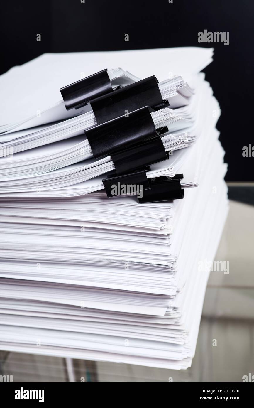 A stack of office papers, some of which are fastened with black binders ...