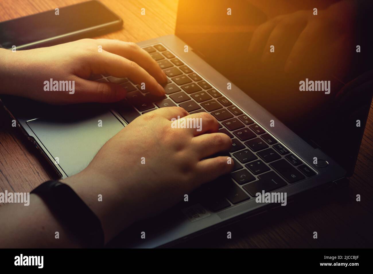 Closeup image of hands typing on laptop with warm light ambient ...