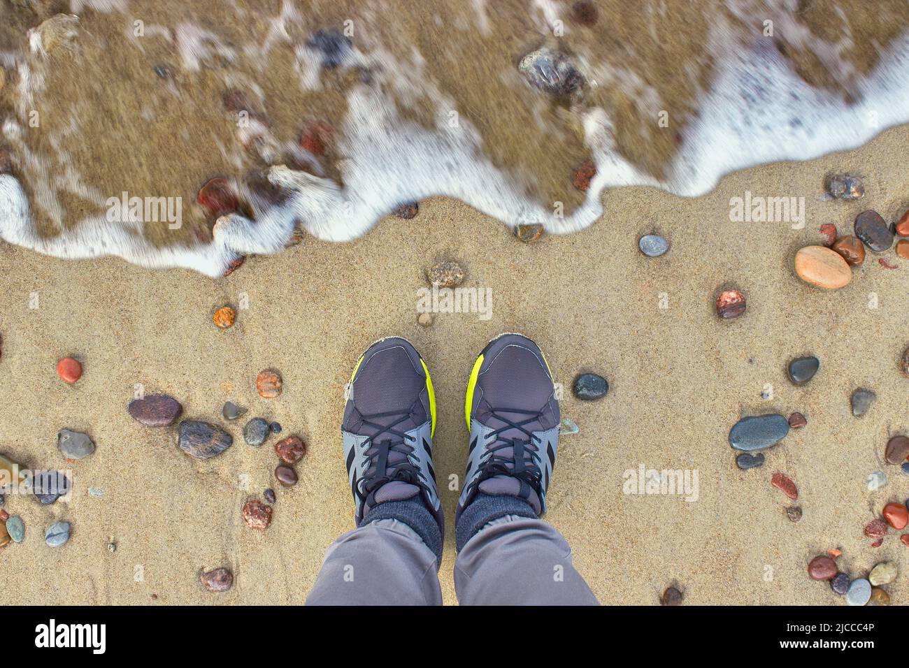 Feet in sneakers on the beach. The wave is coming Stock Photo - Alamy