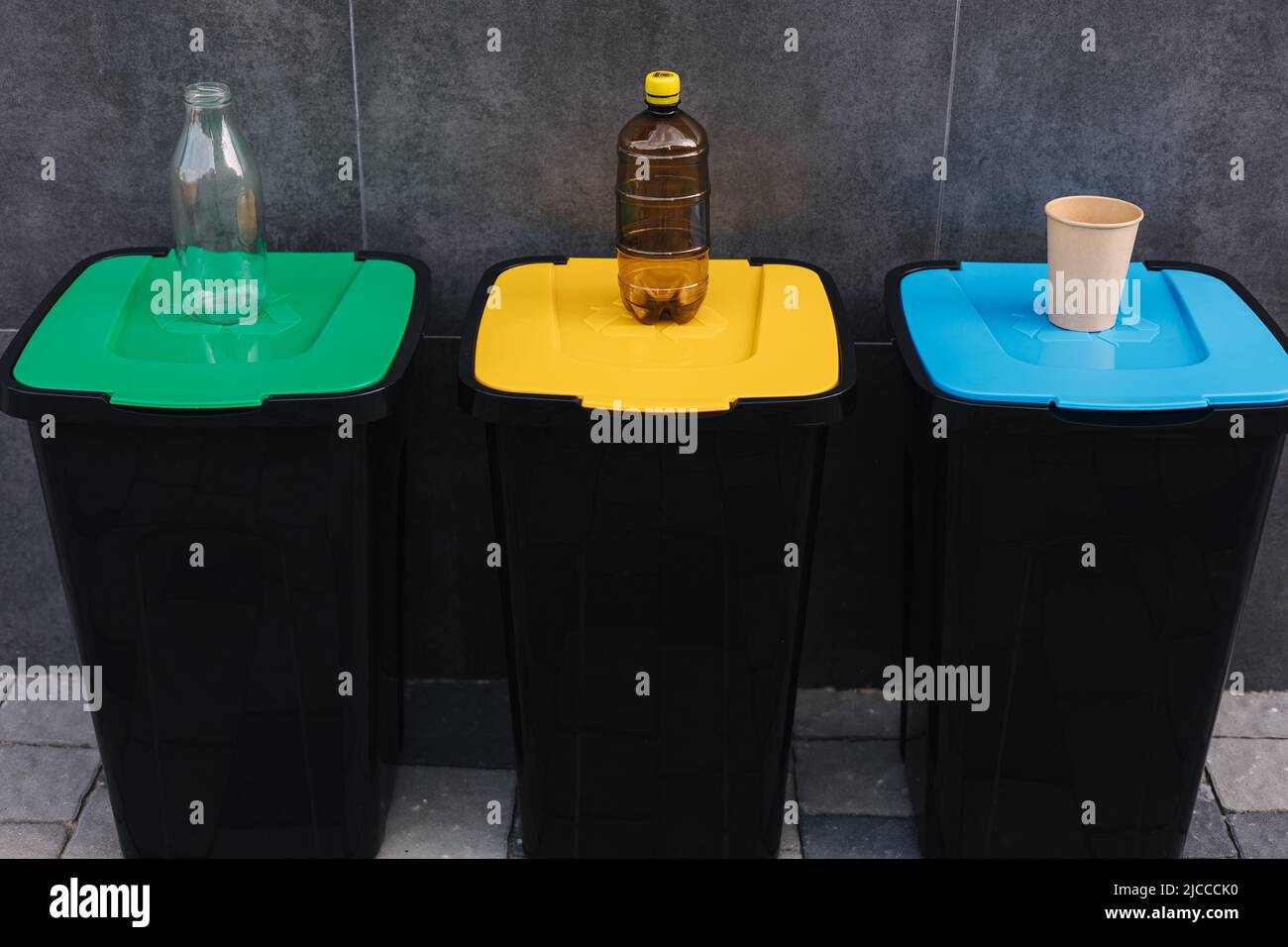 Outdoors in the park is recycling bins different colours. Tree closed ...