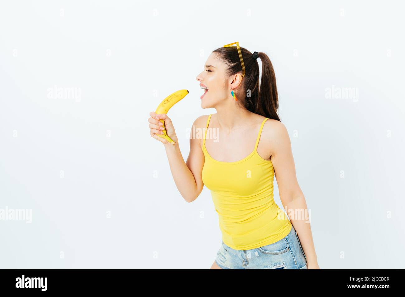 Side view young woman singing using banana as microphone, white studio ...