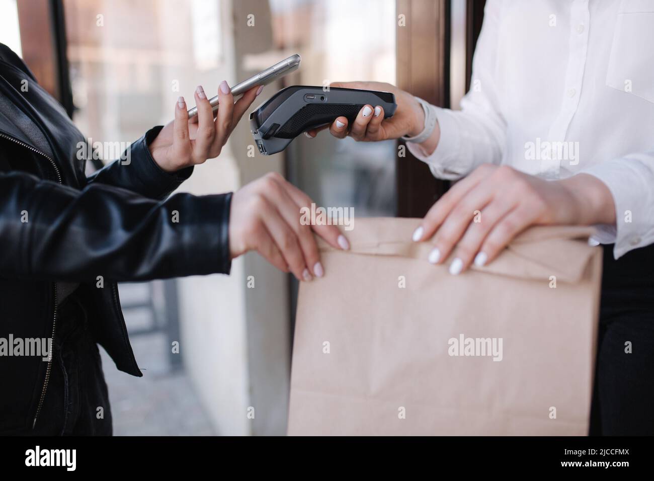 Closeup of female standing outdoors by cafe and paying with smartphone ...