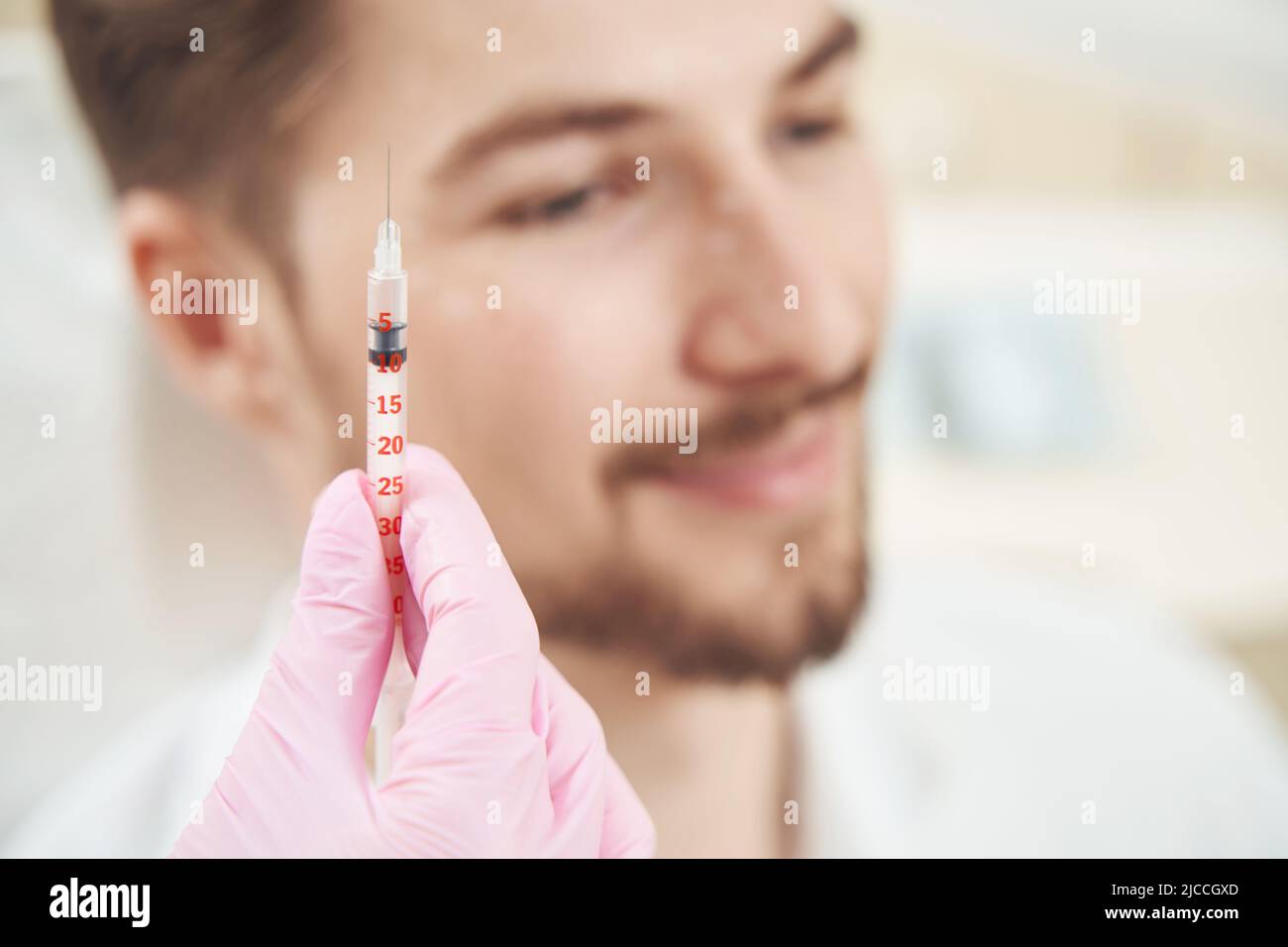 Person holding syringe with injection before patient in background ...
