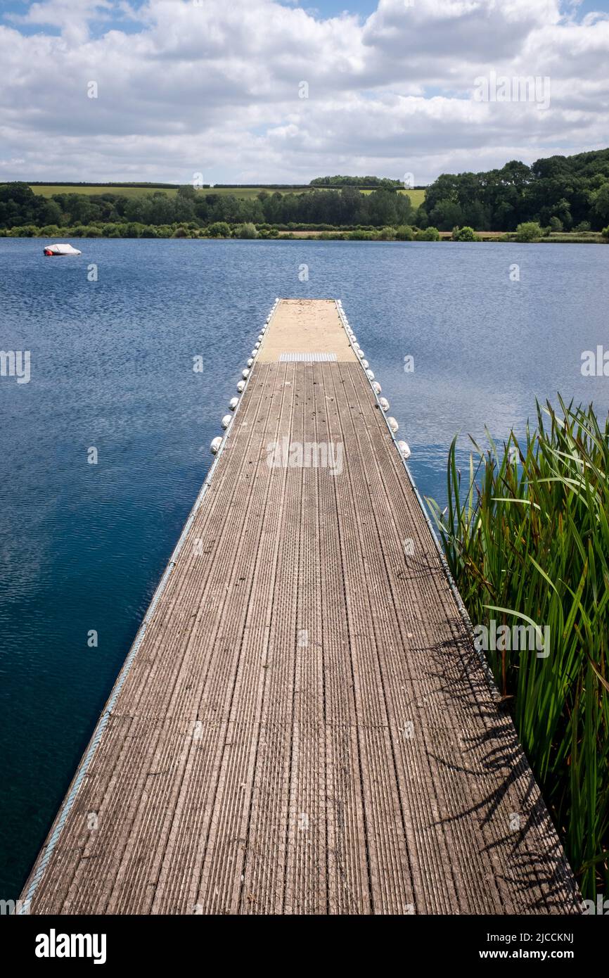 Symmetric photo of a small jetty on a lake with trees on the far shore ...