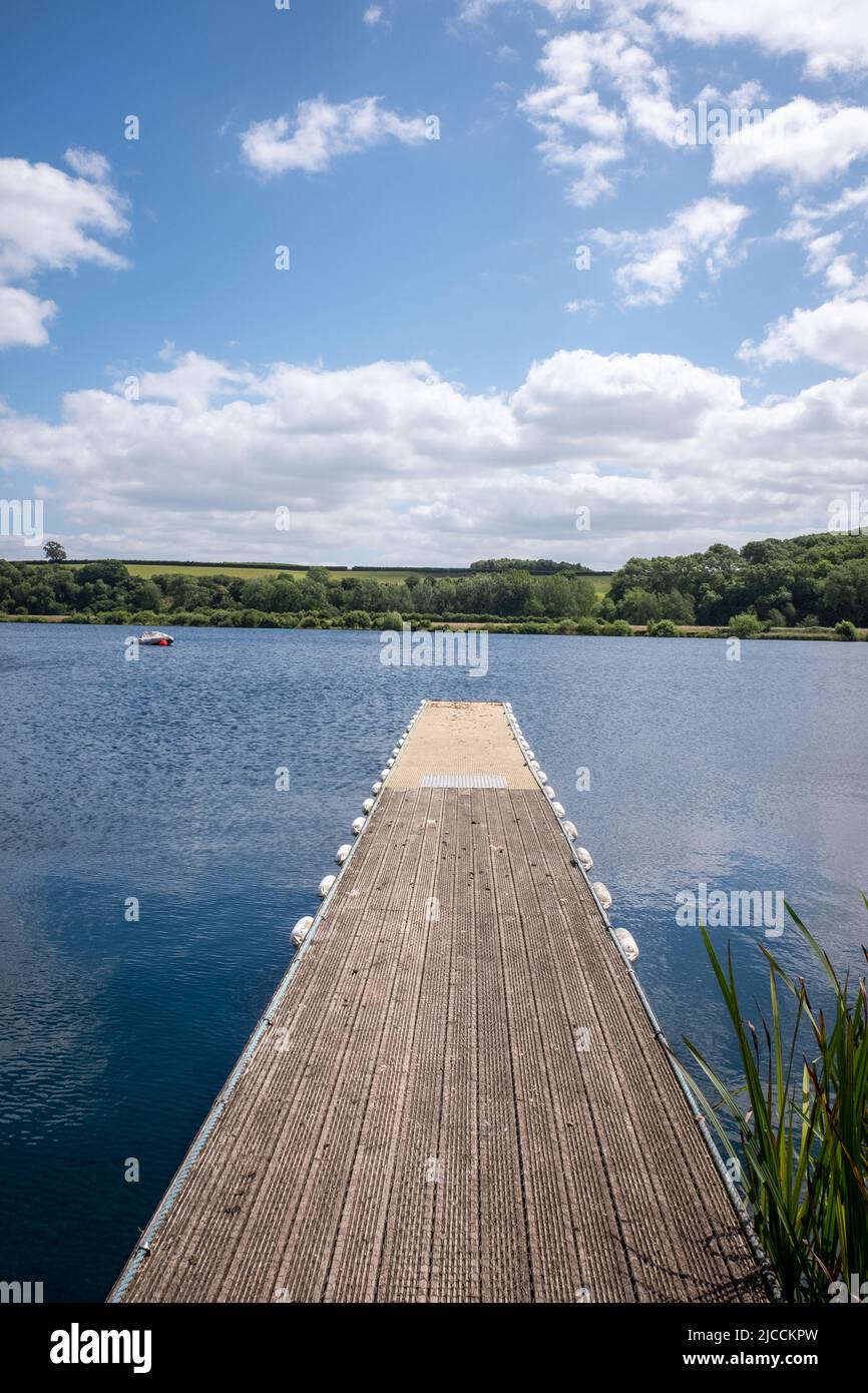 Symmetric photo of a small jetty on a lake with trees on the far shore ...