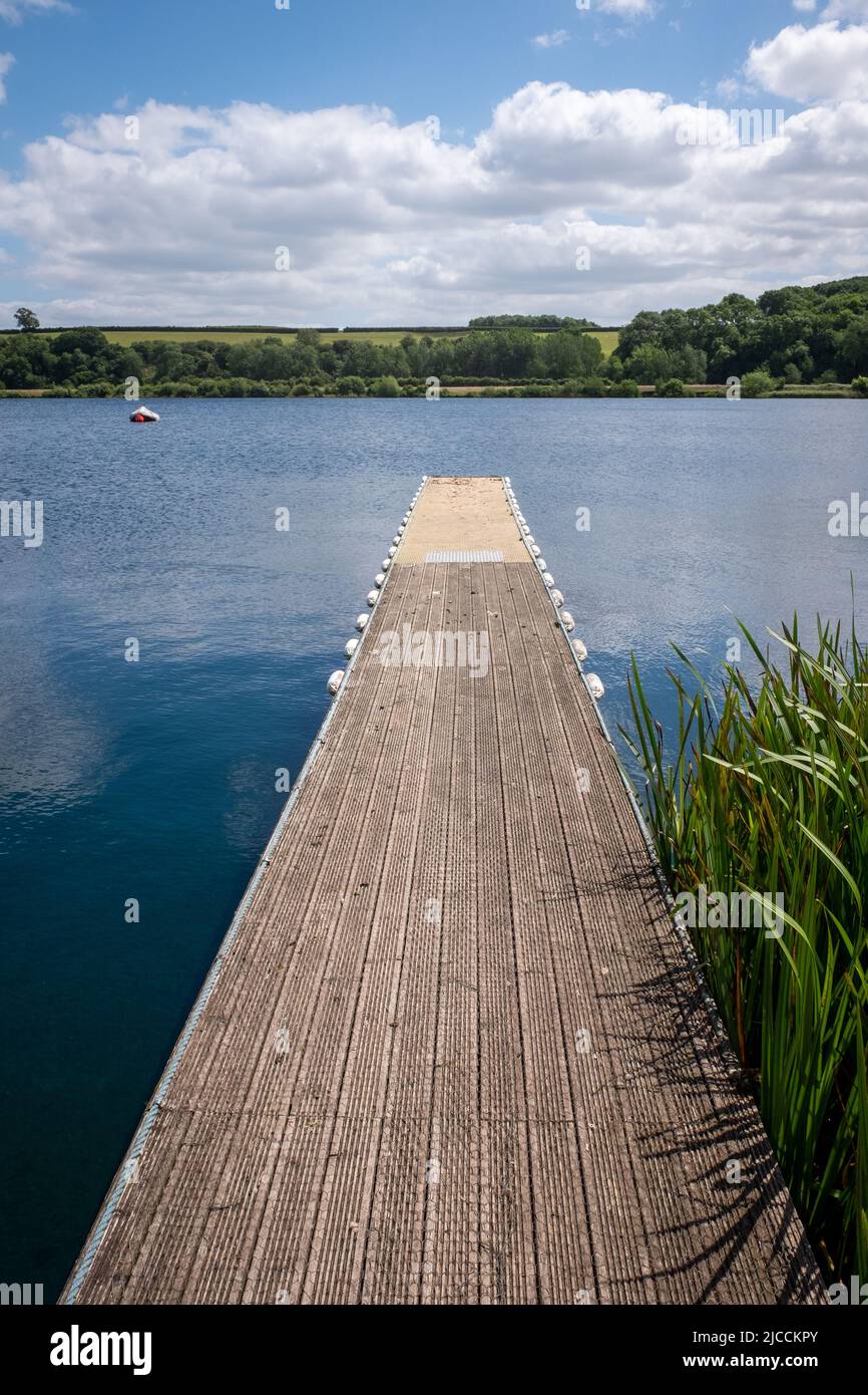 Symmetric photo of a small jetty on a lake with trees on the far shore ...