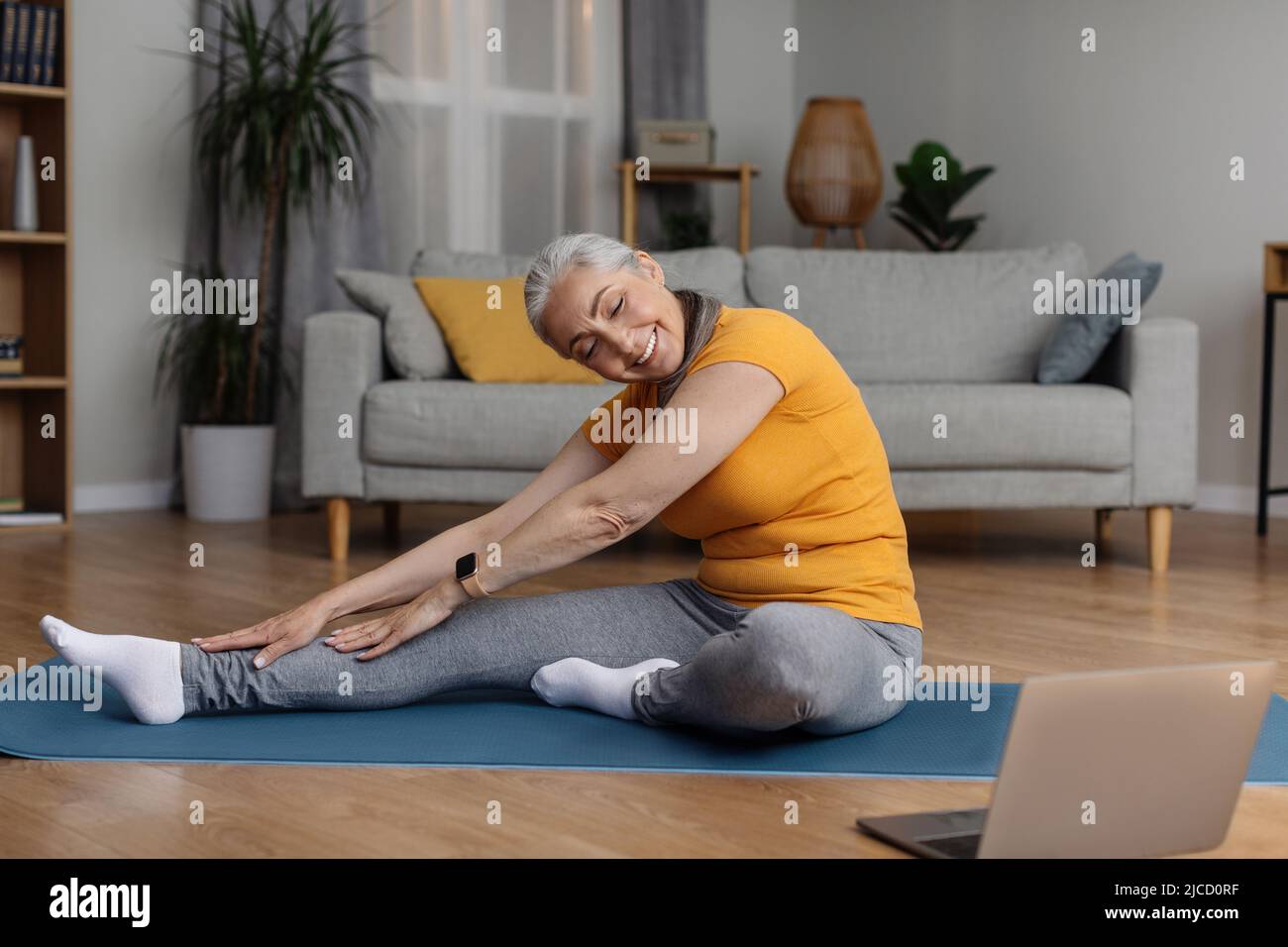 Athletic senior woman stretching her leg on yoga mat, workig out at ...