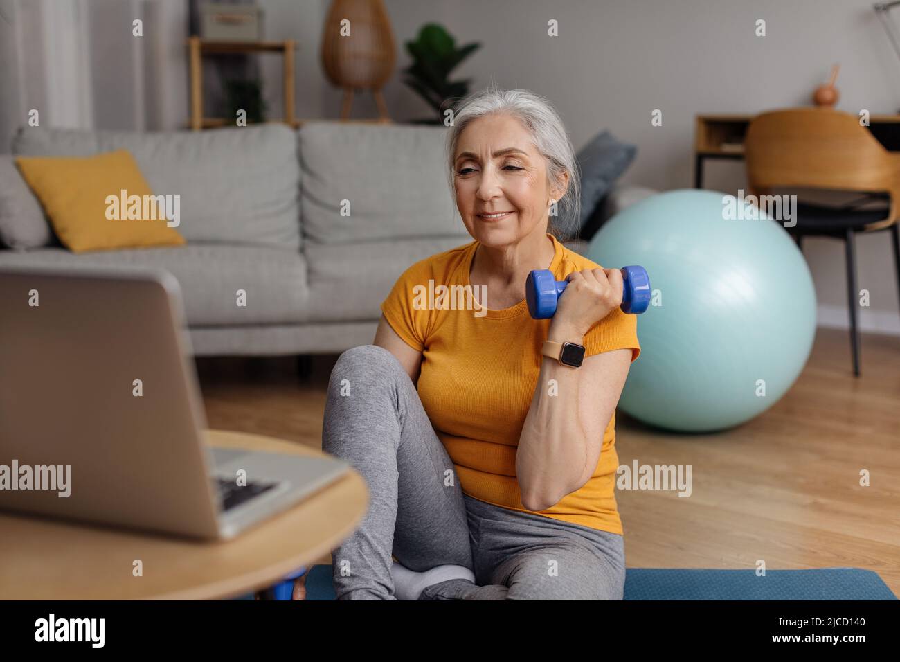 Domestic online training. Senior woman doing exercises with dumbbells ...