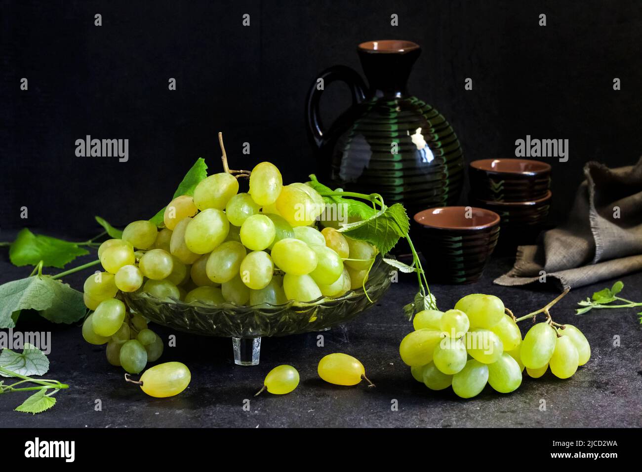 Fresh ripe grapes with leaves in a fruit bowl and ceramic jar and ...