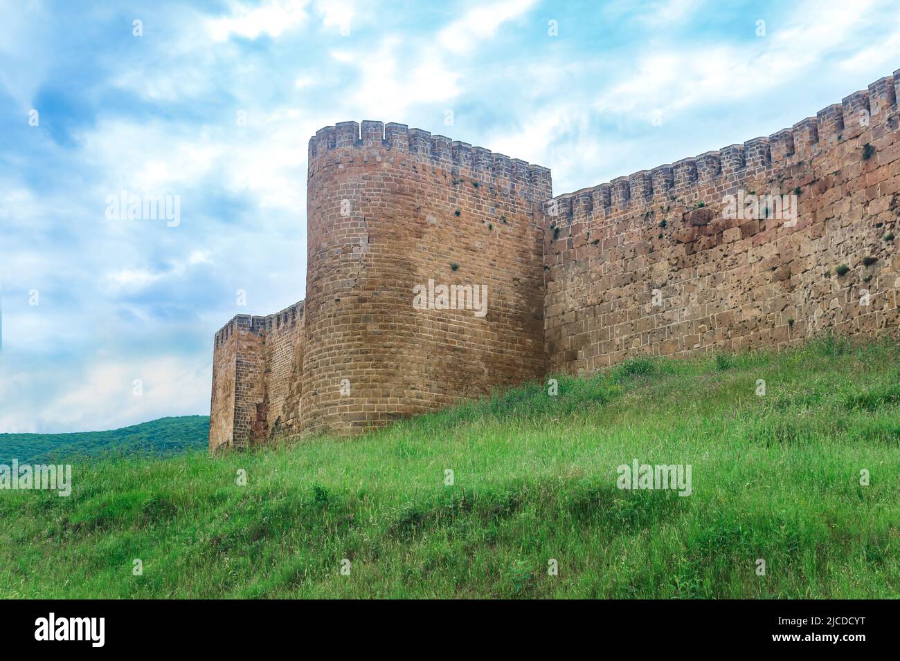 wall of a medieval fortress above a rampart overgrown with grass ...