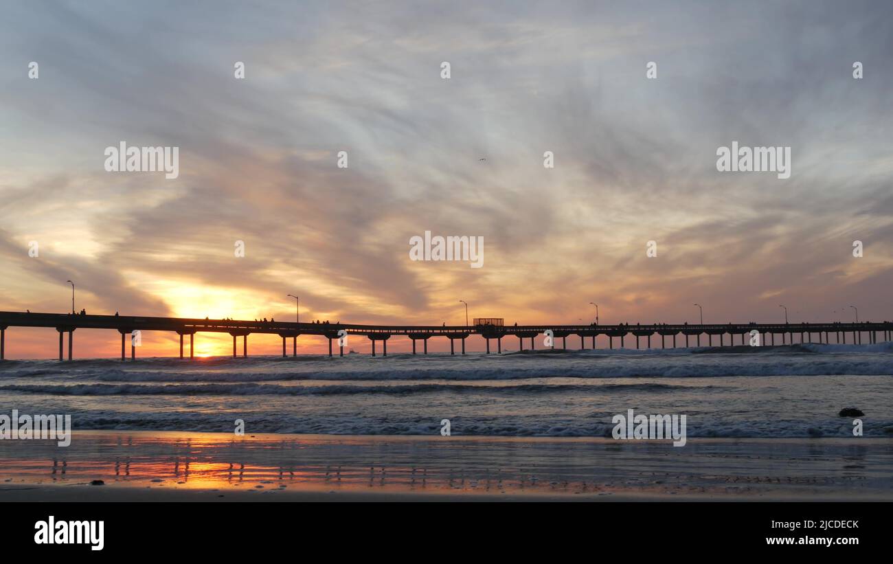 Silhouette of people walking, pier on piles in sea water. Ocean waves ...