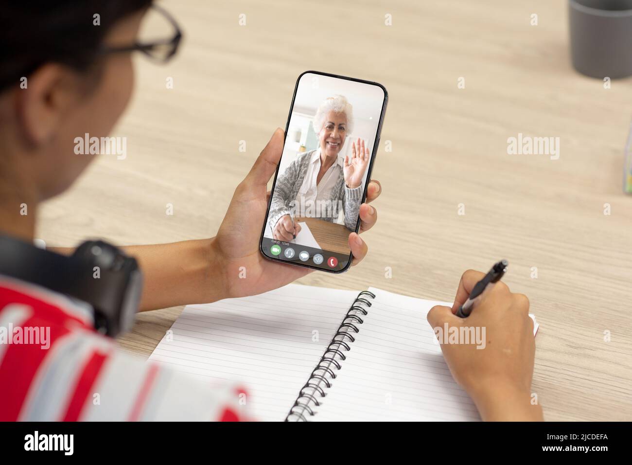 Asian businesswoman writing notes while video conferencing with senior ...