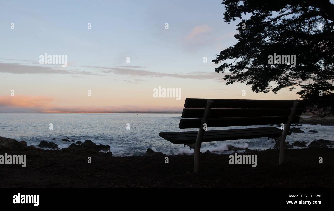 Ocean beach, empty bench silhouette on shore, sea water waves, Monterey ...