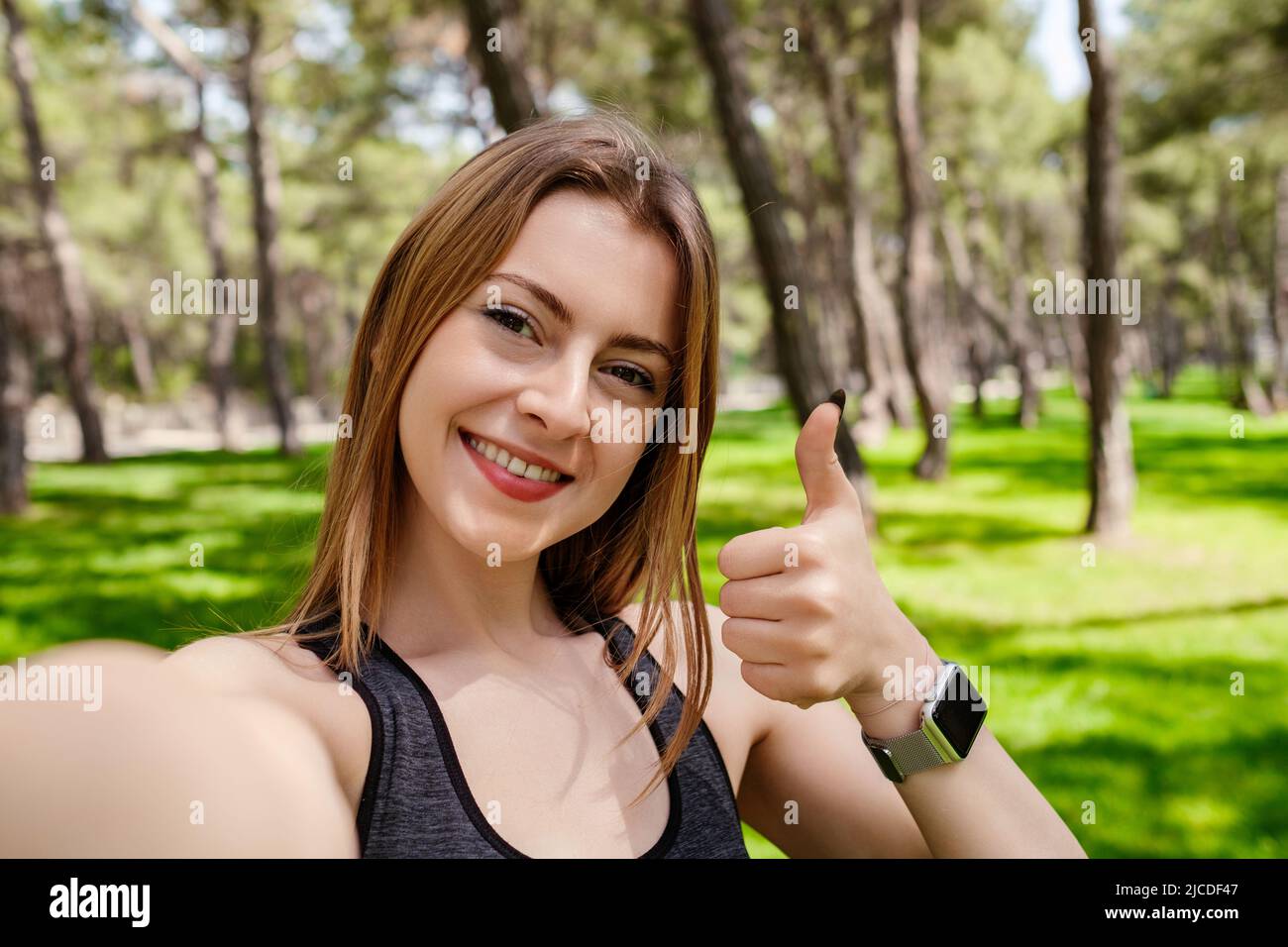 Happy brunette woman wearing black sports bra standing on city park ...