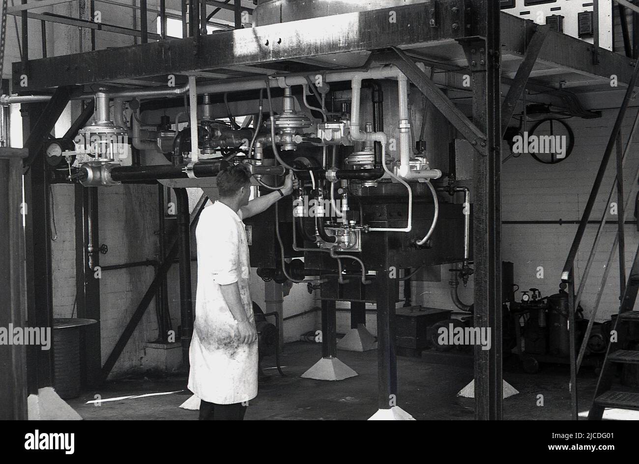 1960s, historical, a male operative in overalls adjusting a value on a ...