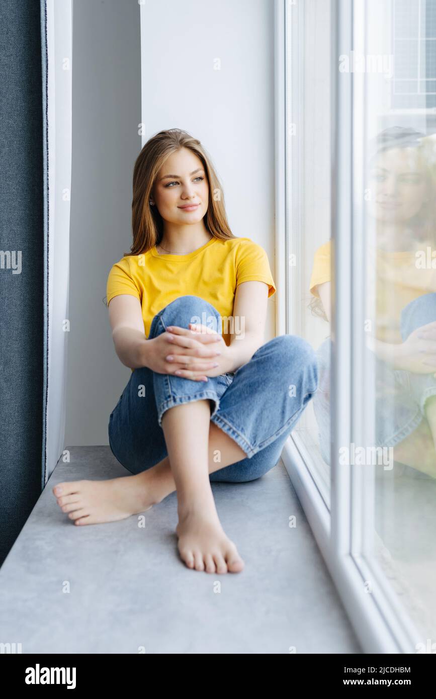 Young woman looking through the window with a city view, sitting on a ...