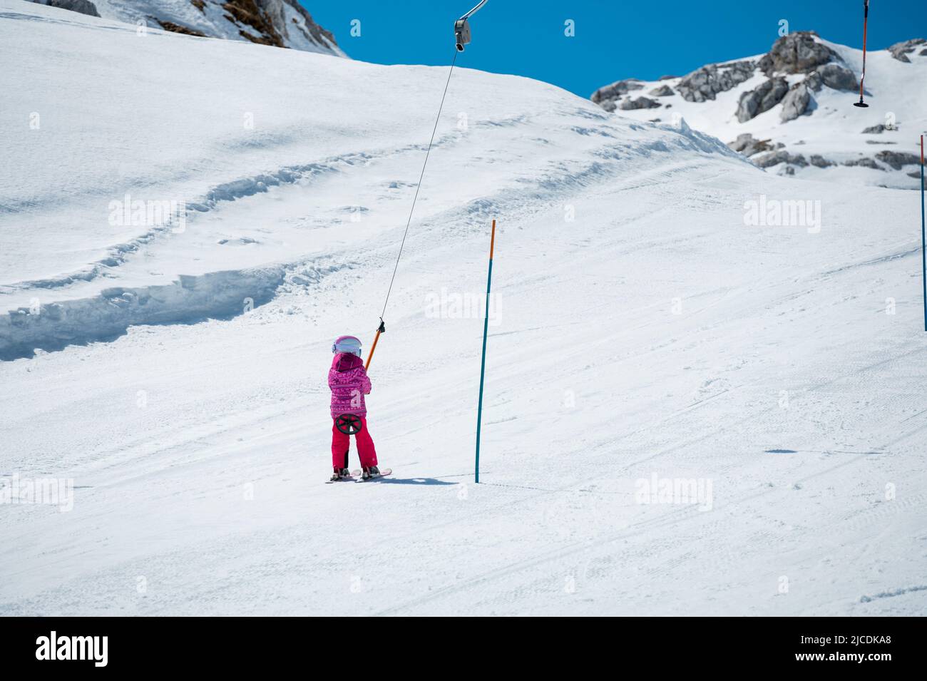 Small cute girl taking a ski lift and learning to ski on a sunny day ...