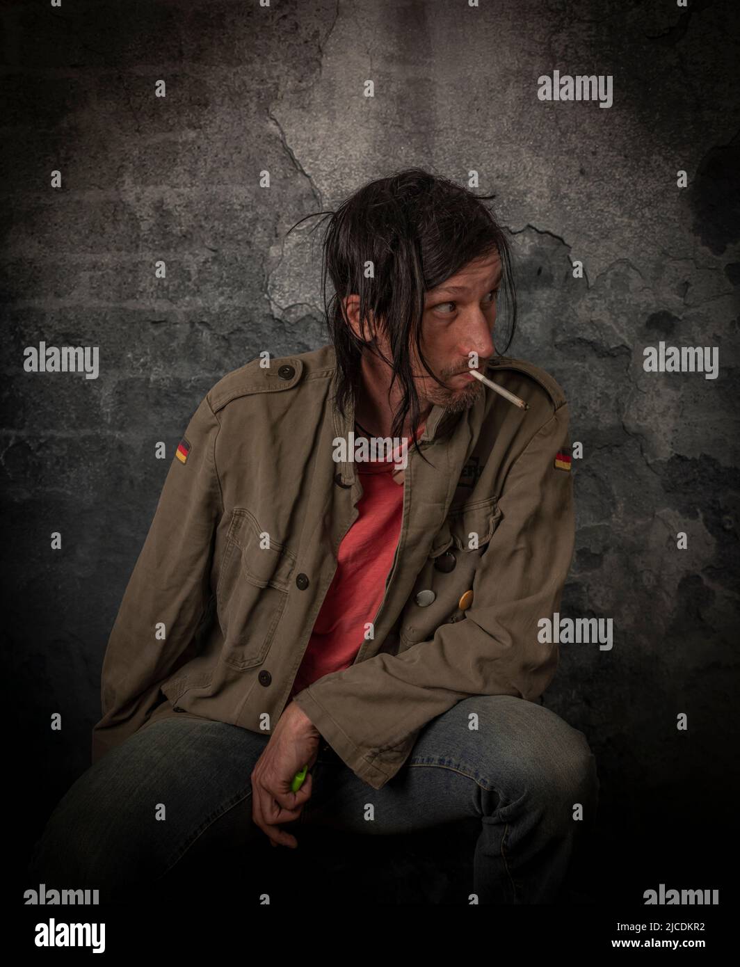 Junkie man with black hair and bottle with joint near old stone wall ...