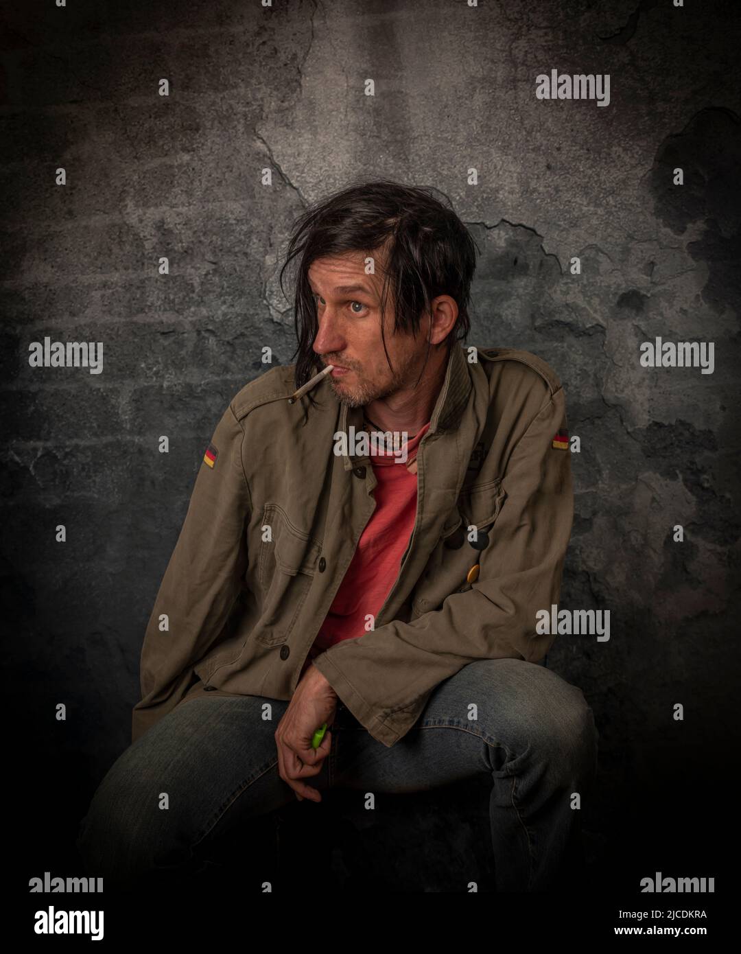 Junkie man with black hair and bottle with joint near old stone wall ...