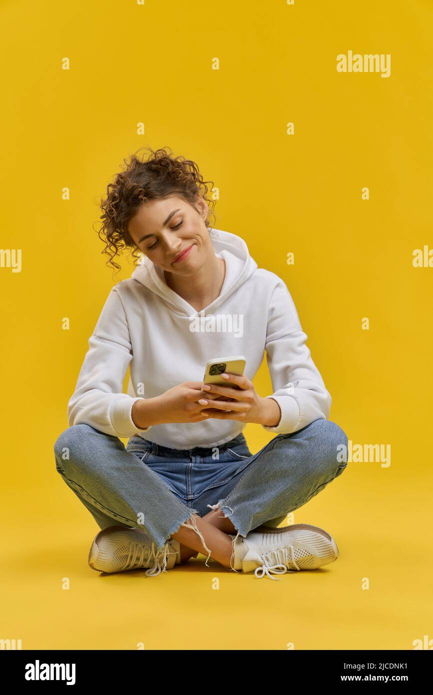 Smiling teen surfing internet with smartphone, while sitting on floor ...