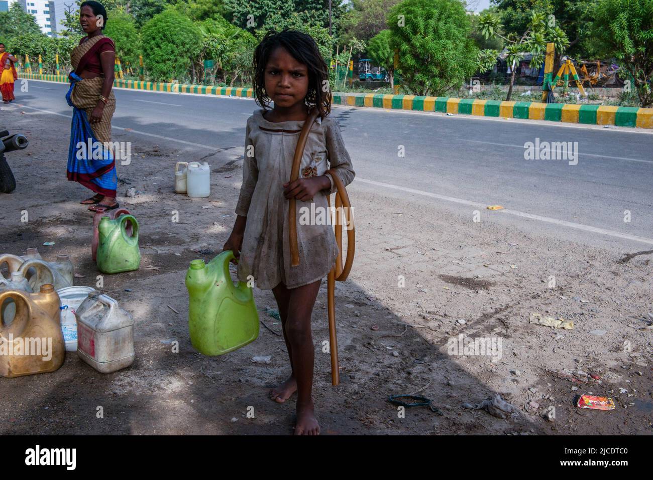 A young girl carries a container and waterpipe as she goes to collect ...