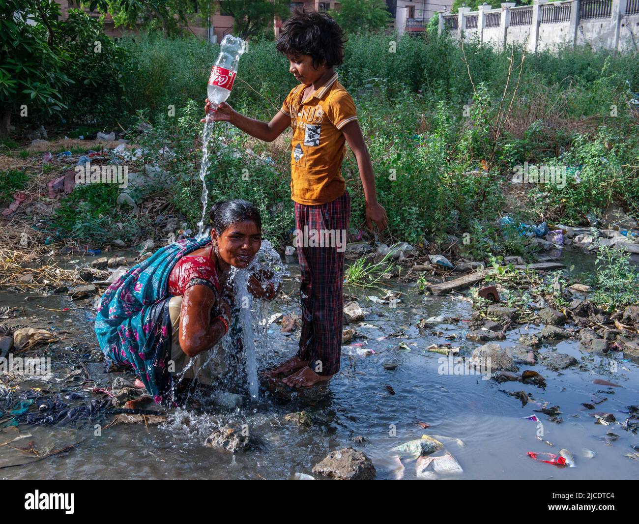 A child pours water on a woman next to a water pipeline leakage in ...