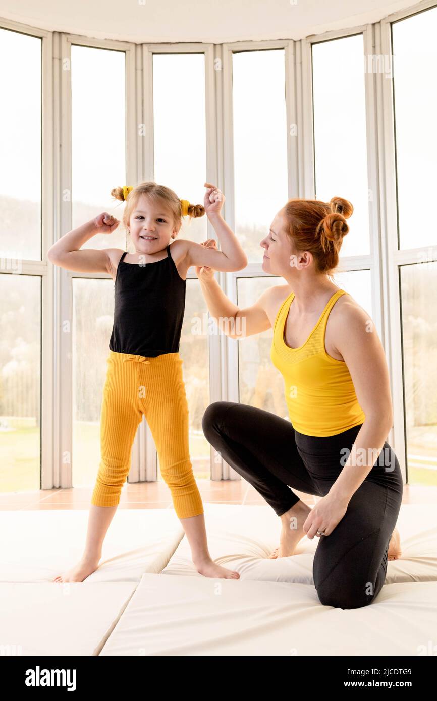 Young fit mom and her daughter in matching clothes, showing muscles ...