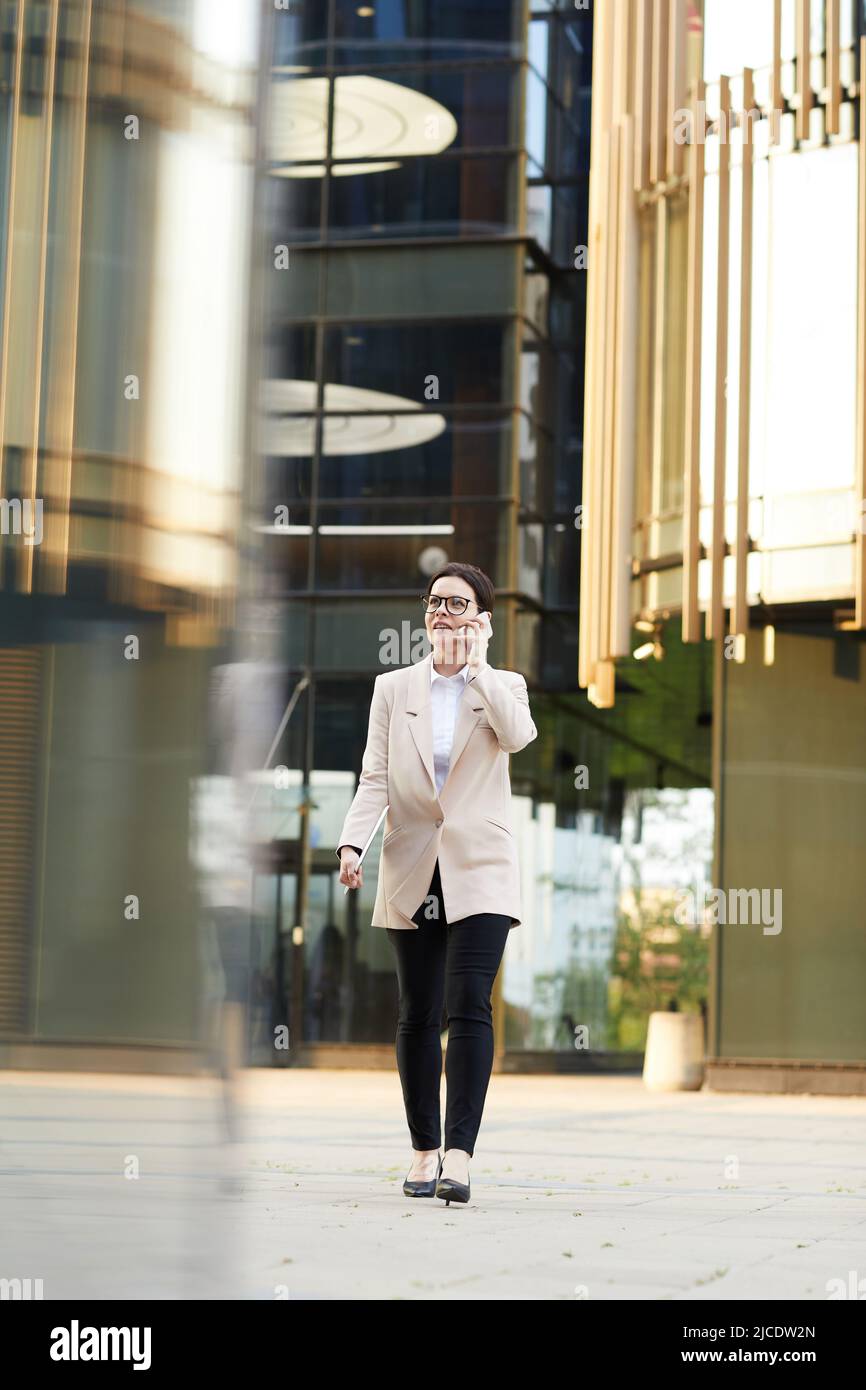 Pensive stylish lady in eyeglasses walking over city street and ...