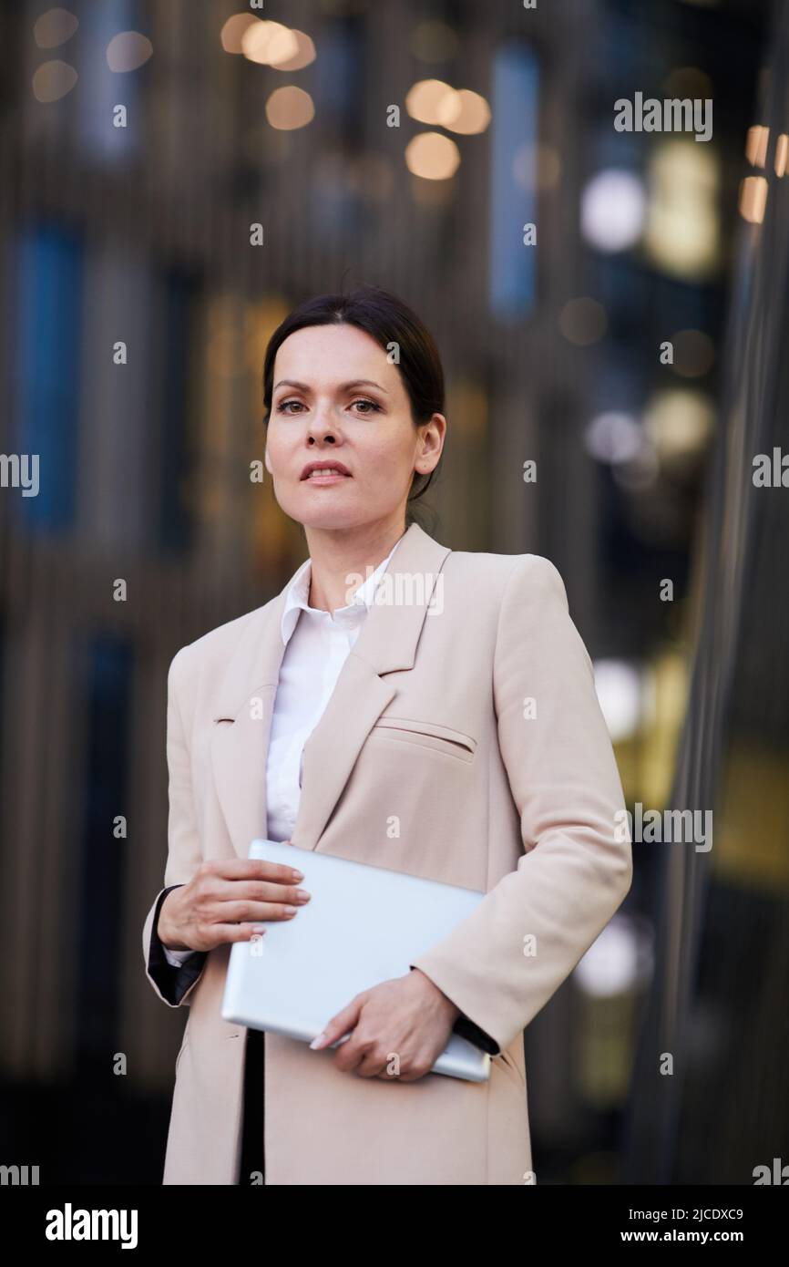 Portrait of content successful female business expert in elegant jacket holding portable gadget ...