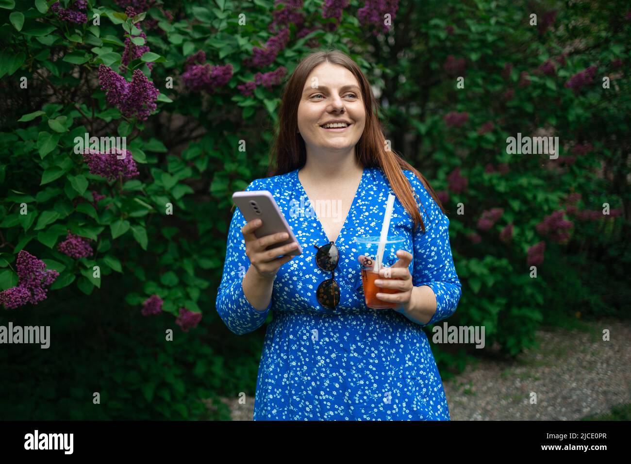 Young beautiful woman in bright blue dress holding plastic cold tea cup ...