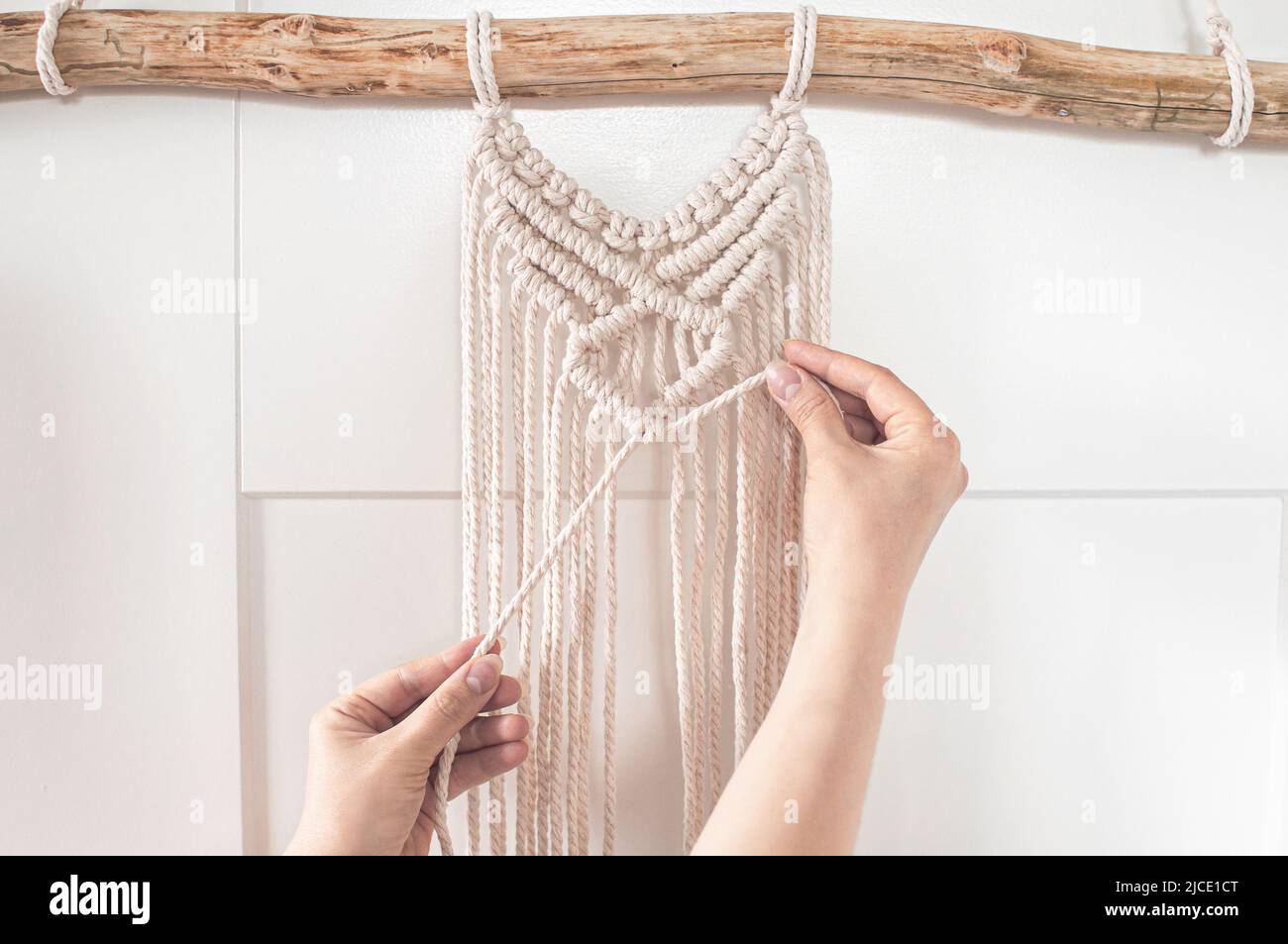 girl weaves a macrame pattern from natural white cotton threads for a ...
