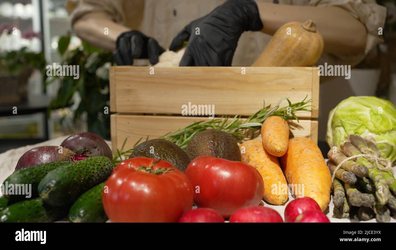 Shop worker carefully loads wooden box with variety of fresh vegetables ...