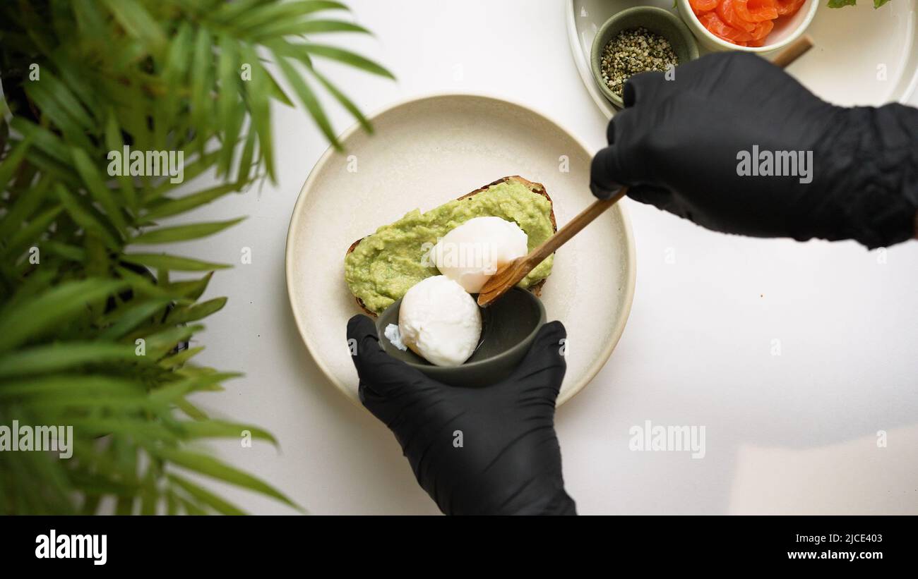Cook in black rubber gloves puts poached eggs on toast with guacamole ...