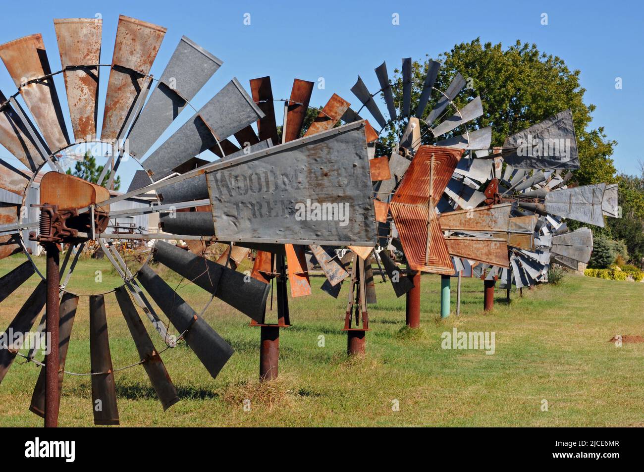A collection of old metal windmills is displayed at a rural property ...