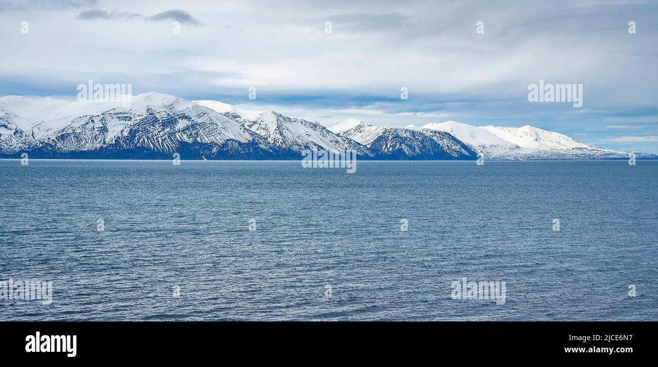 Idyllic view of seascape and snowcapped mountains against cloudy sky ...