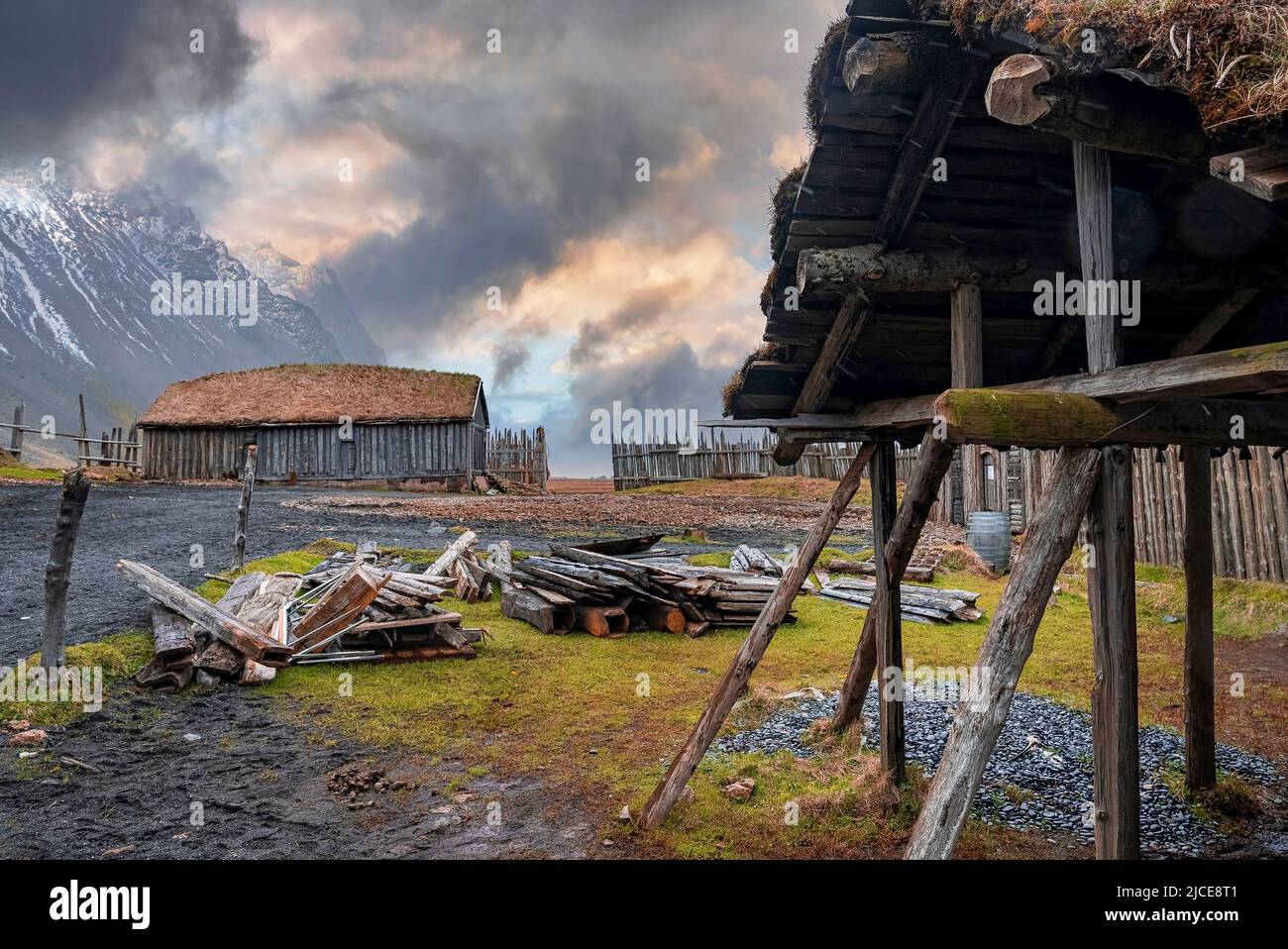 Logs by shed and traditional houses surrounded by fence in old Viking ...