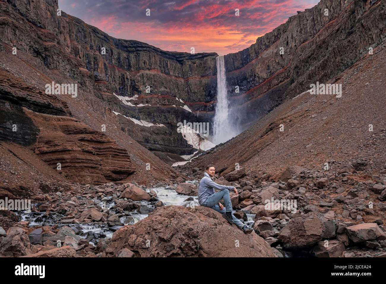 Tourist sitting on rock against Hengifoss waterfall amidst mountains at ...
