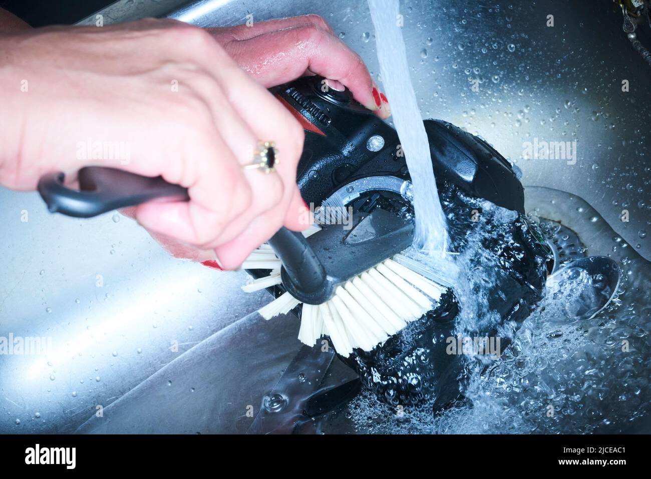 Female hands washing dslr camera as dirty dishes running water in the ...