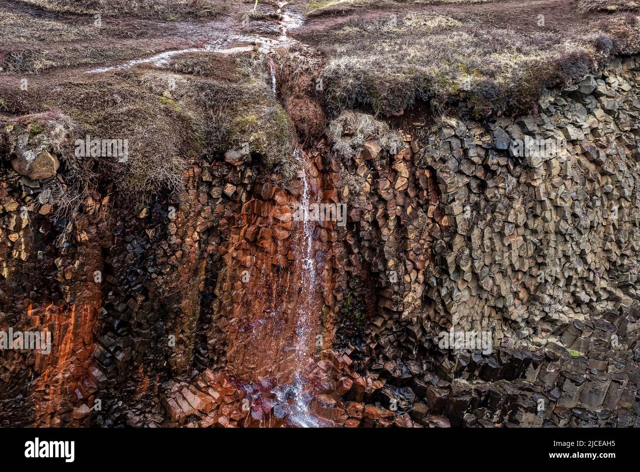 View of small waterfall falling over basalt rock columns on cliff in ...
