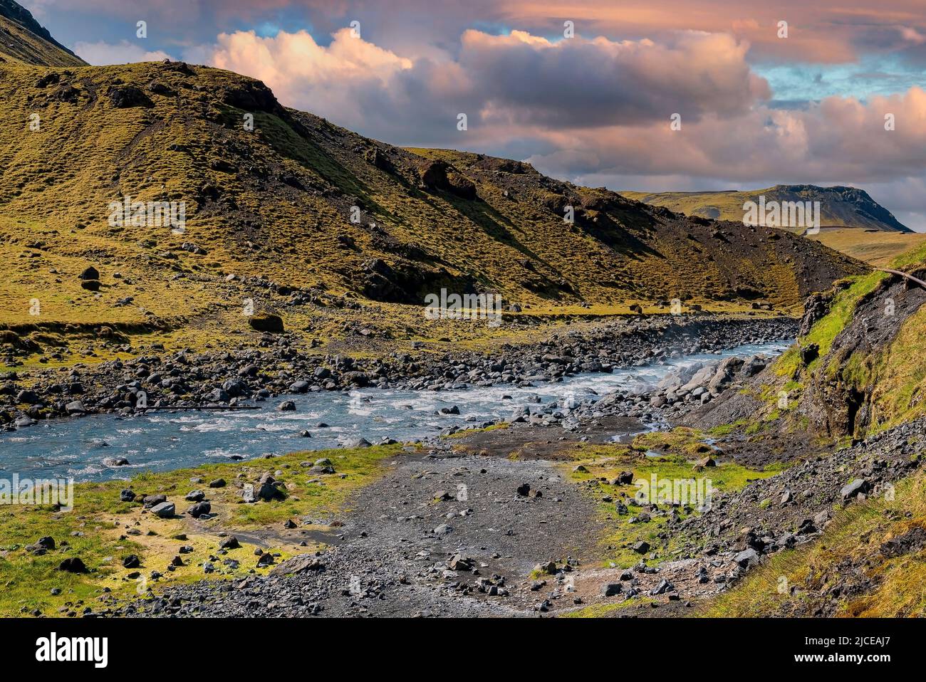 Beautiful stream flowing amidst mountains at Seljavellir against cloudy ...