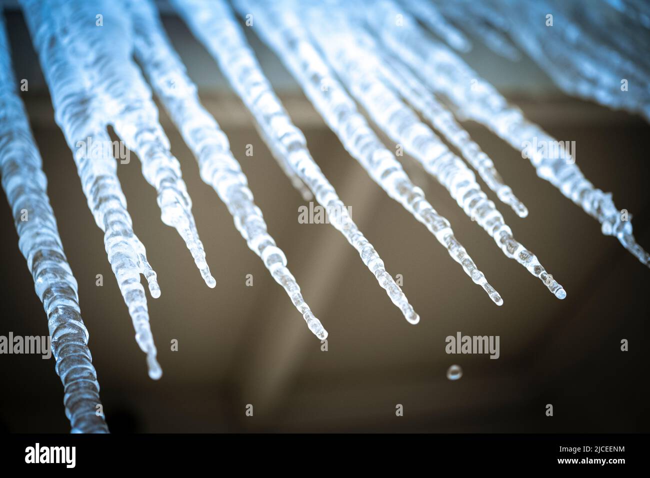long icicles melting from a roof with one drop falling Stock Photo - Alamy