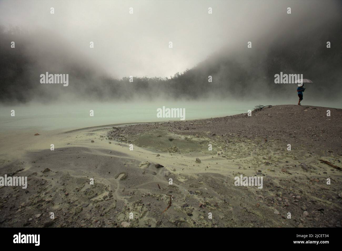 A visitor carrying an umbrella as he is walking on sandy landscape in a ...