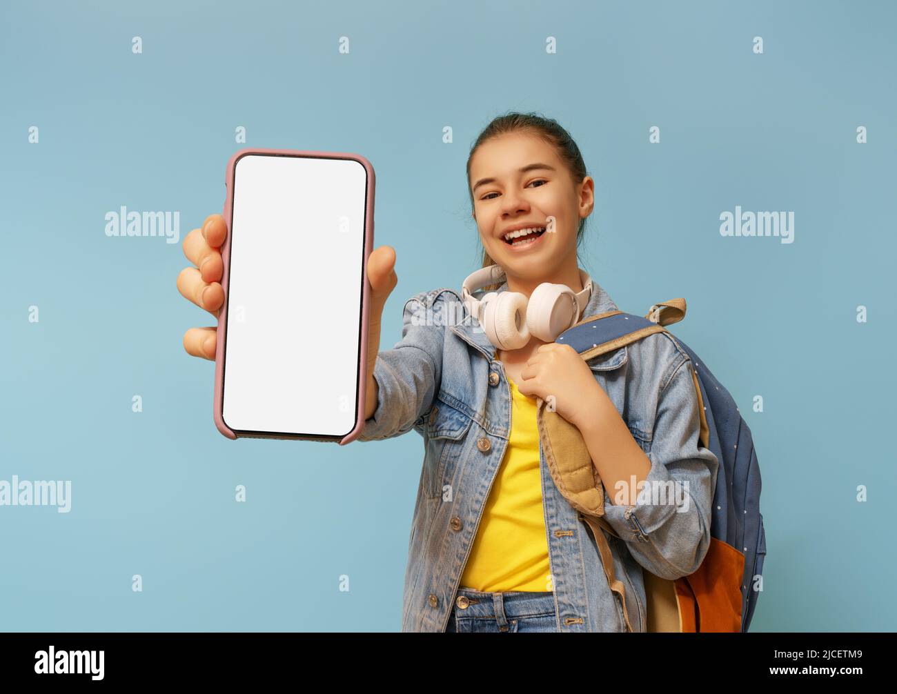 Happy school kid is showing smartphone on background of blue wall ...