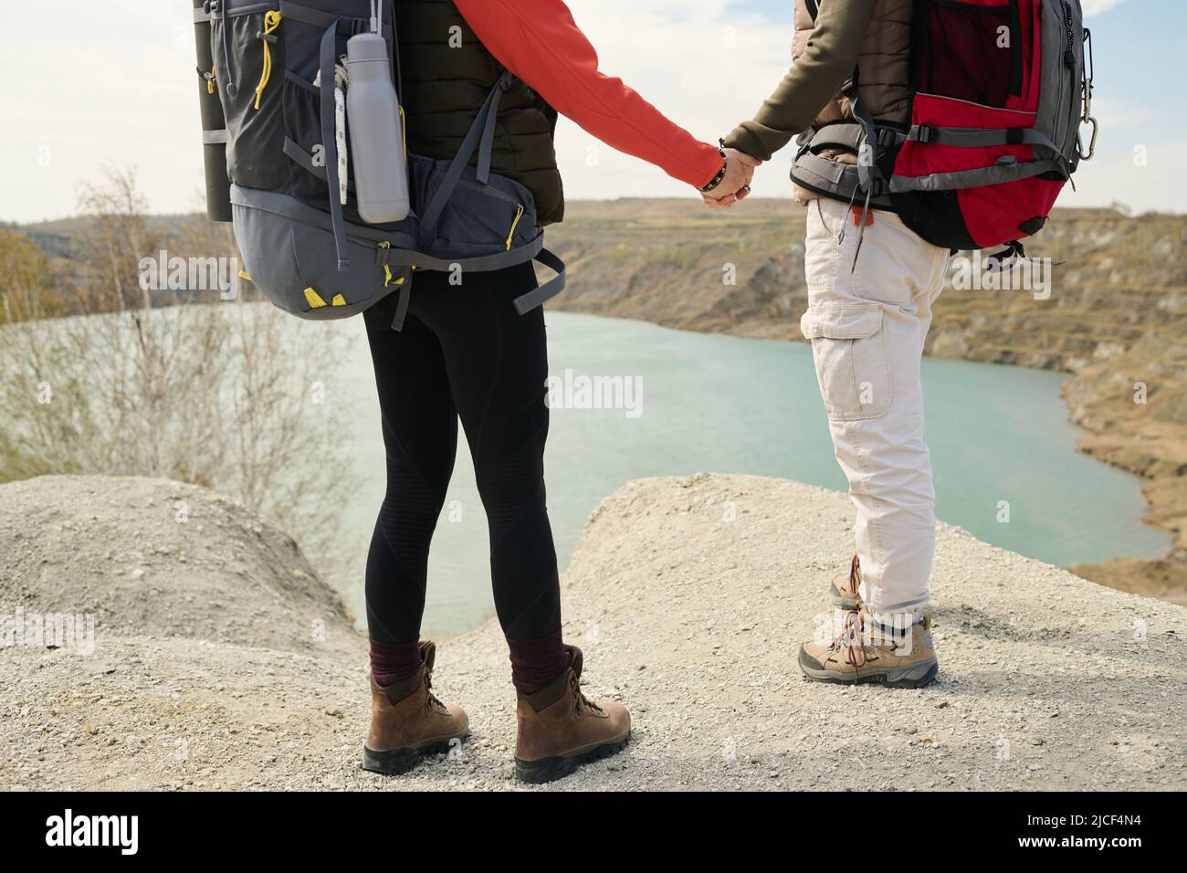 Unrecognizable young women wearing backpacks hiking around quarry lake ...