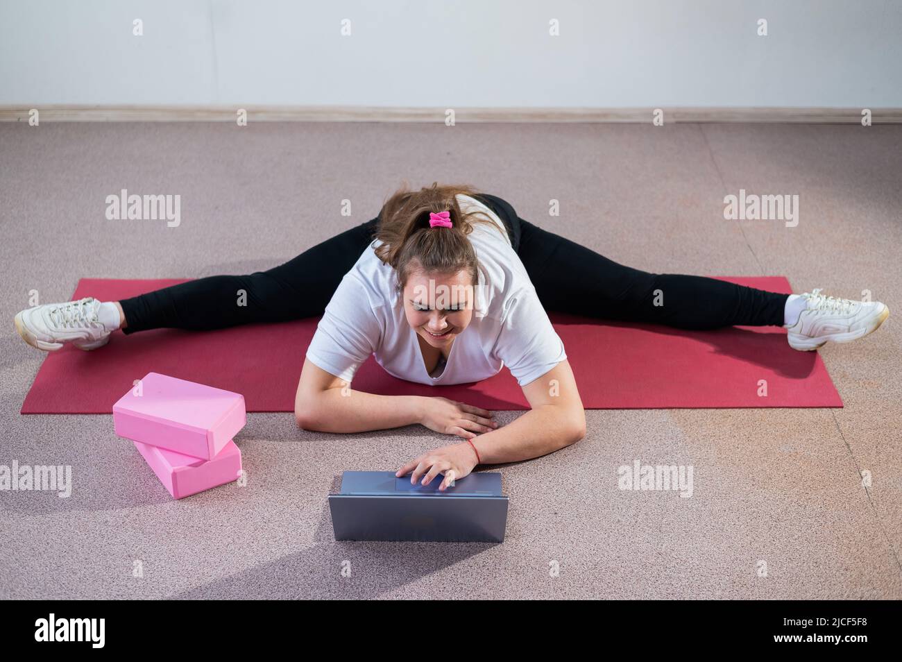 Young caucasian fat woman doing bends on a sports mat and watching a ...