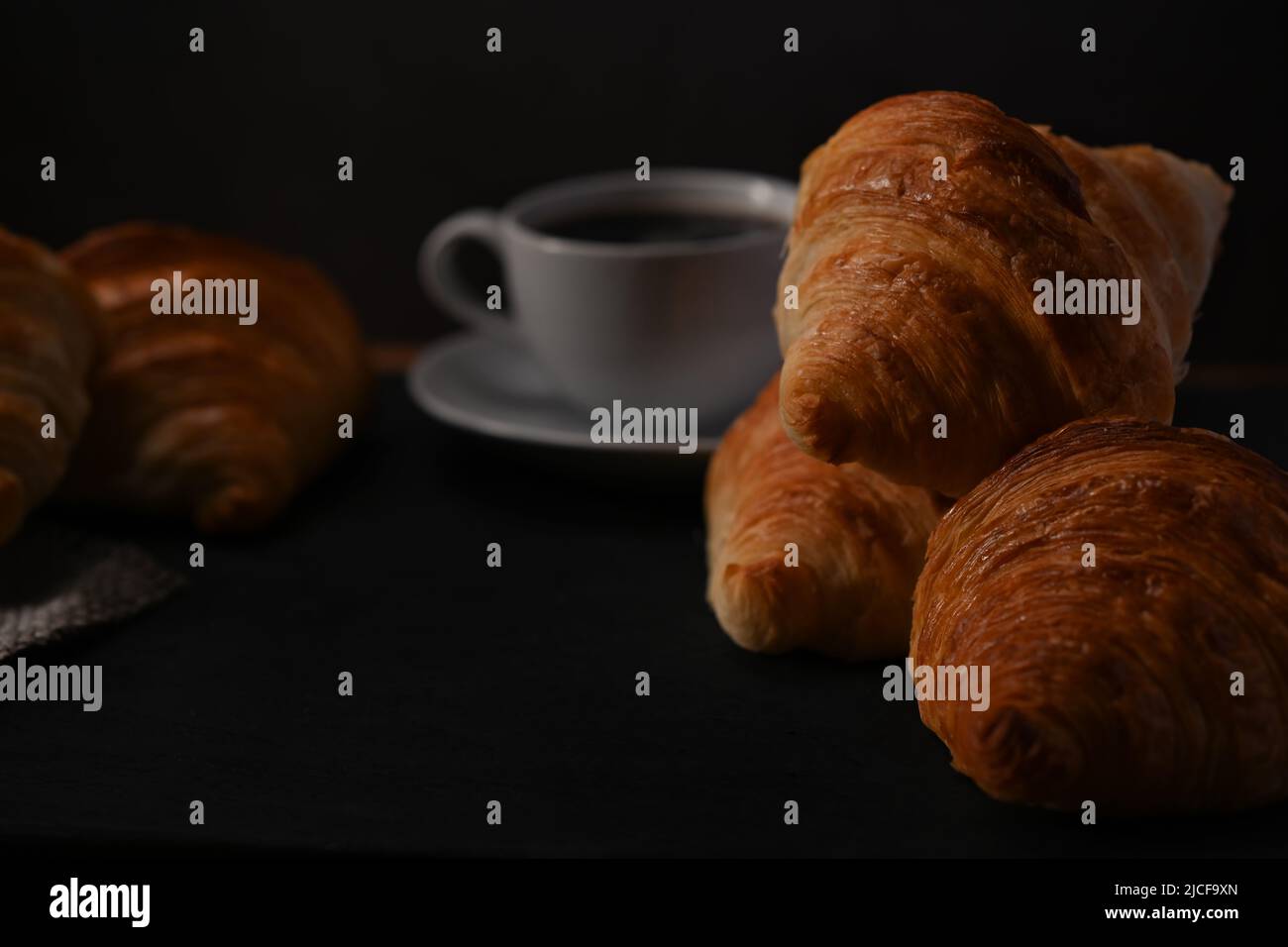 Fresh baked croissant and cup of coffee on black wooden table ...