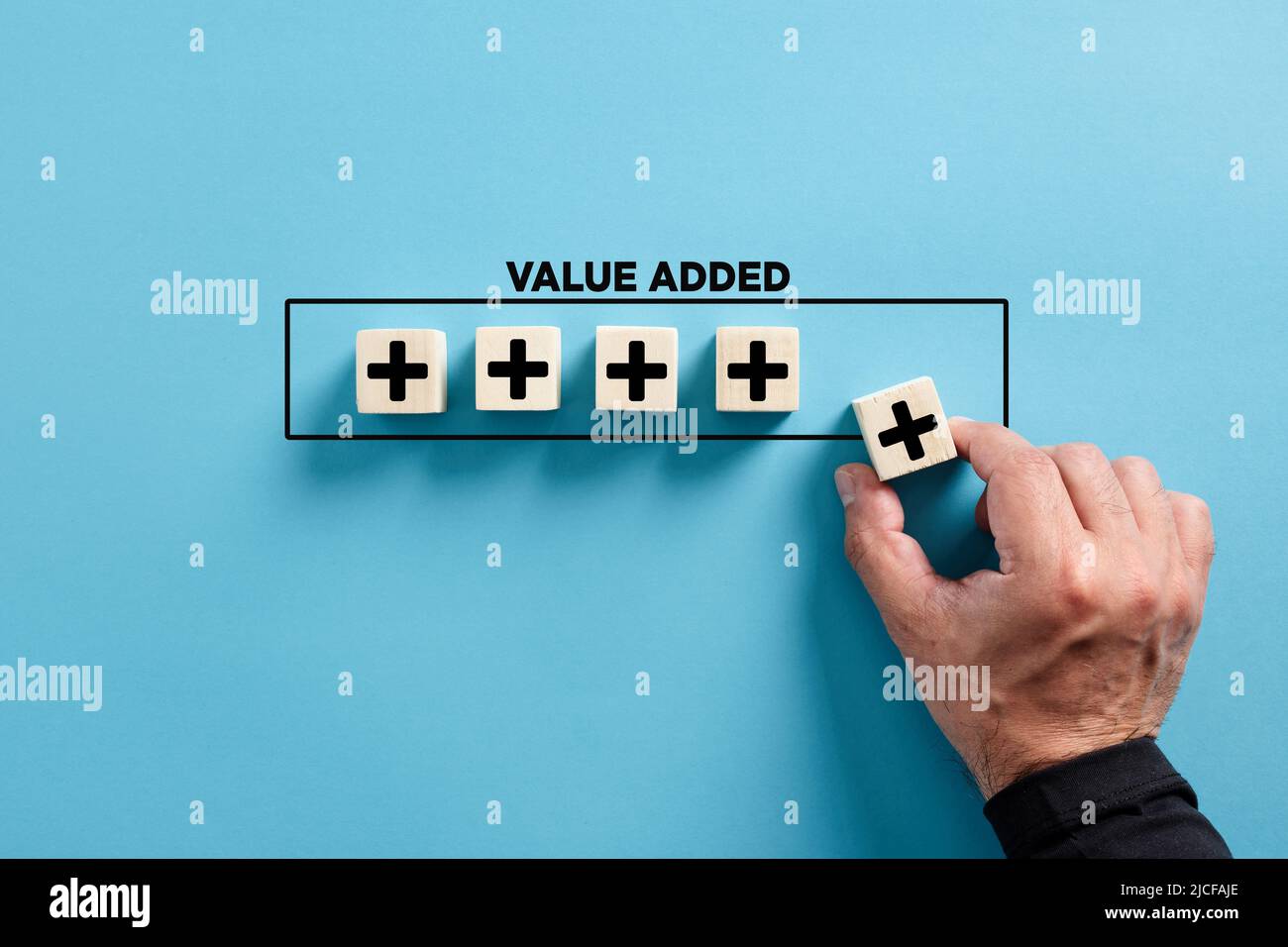 Male hand puts the wooden cube with plus icon with the word value added ...