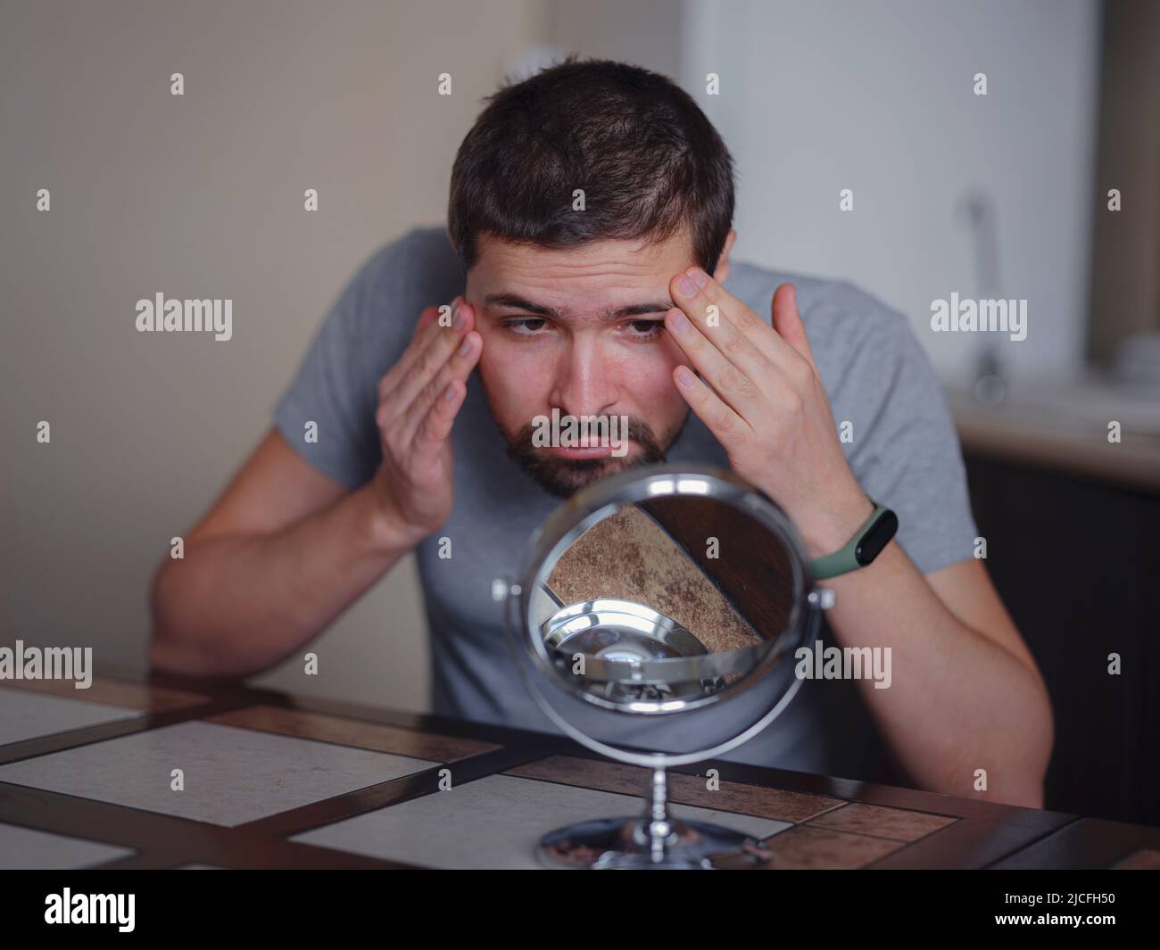 guy checking his skin. Young man looking in mirror touches face with ...