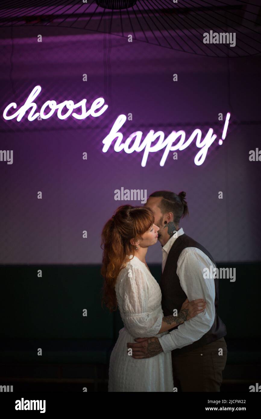 Young couple in love standing together under a neon sign 'choose happy ...