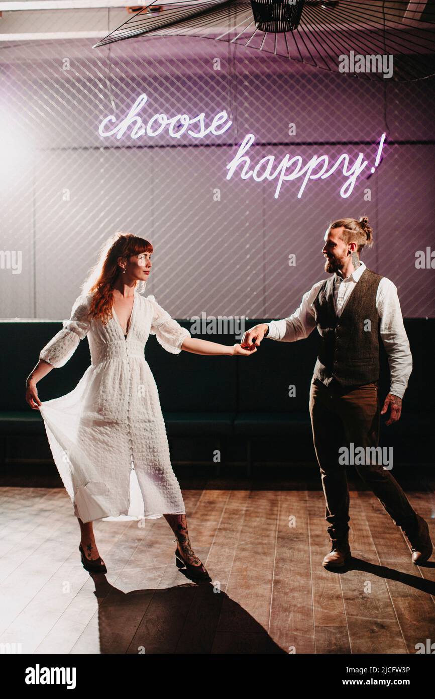 Young couple in love dancing under a neon sign 'choose happy!' Stock ...